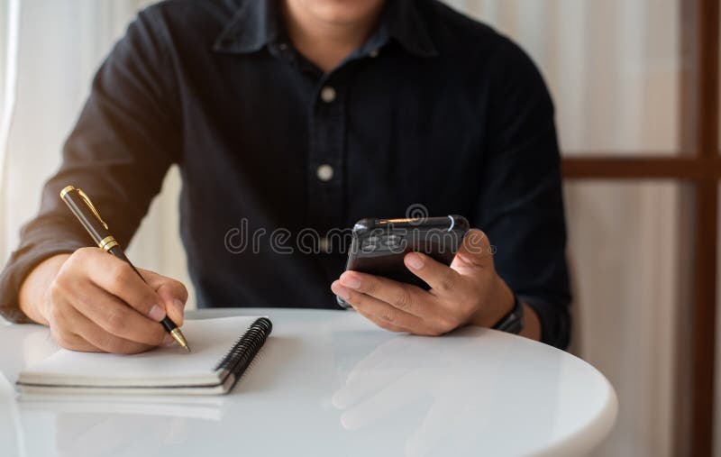 Male Use a Smartphone and Take Notes in the Notebook at the Desk in the ...