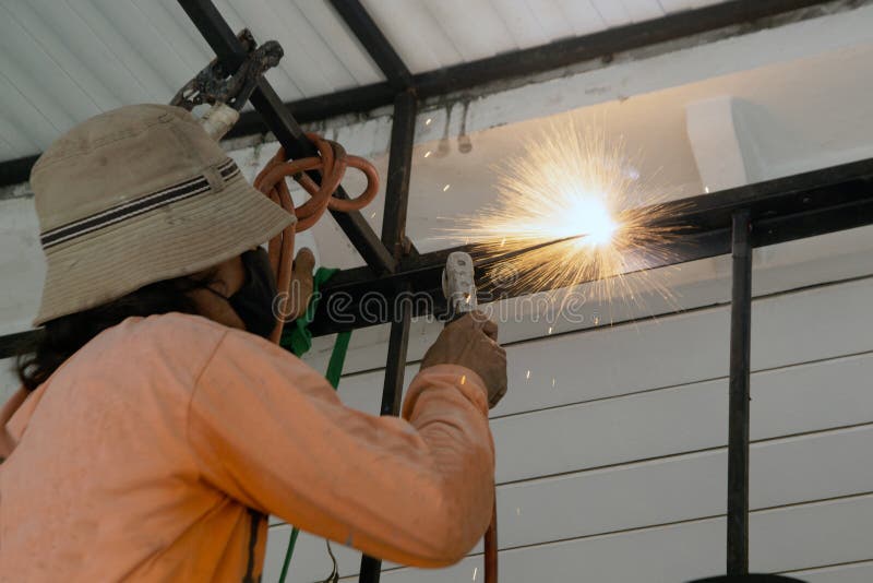 A Male Worker is Welding a Steel Awning on the Ceiling of a House ...