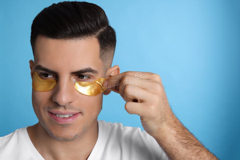 Man Applying Golden Under Eye Patch on Light Blue Background Stock ...