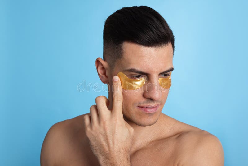 Man Applying Golden Under Eye Patch on Light Blue Background Stock ...