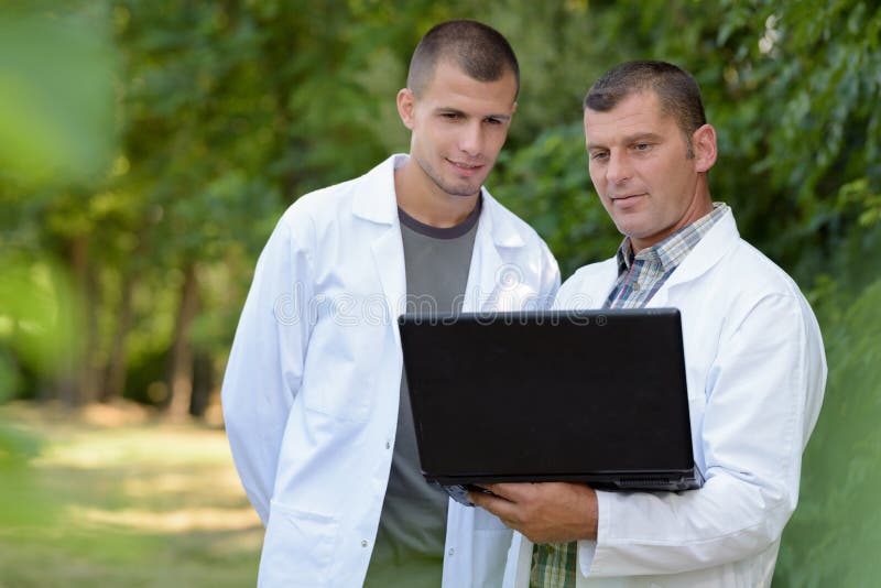 Man and Apprentice in White Coat Using Laptop Stock Image - Image of ...