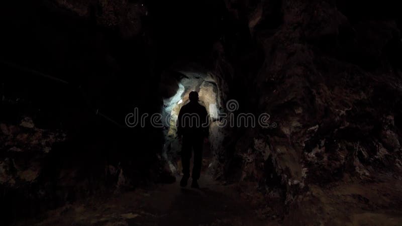 A Man Archaeologist with a Flashlight Walks through a Dark Cave ...