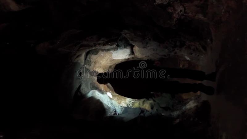 A Man Archaeologist with a Flashlight Walks through a Dark Cave ...