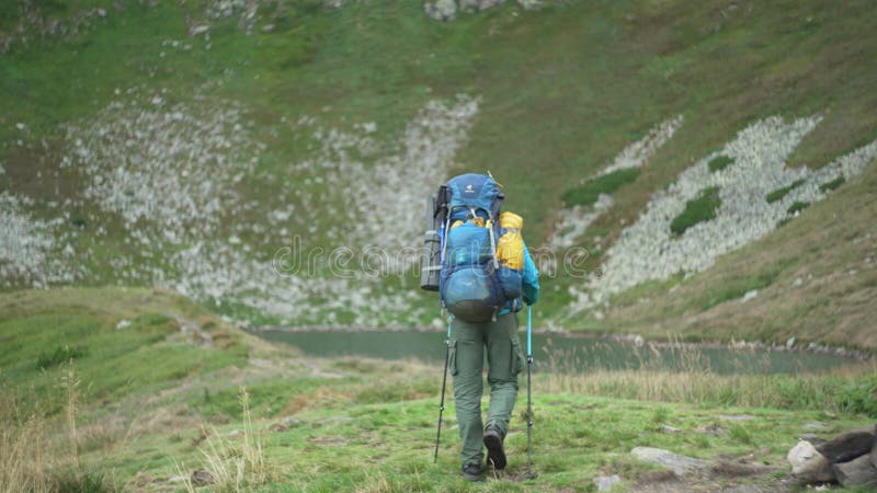A Man with a Backpack, Back View, Approaches a Lake in the Mountains ...