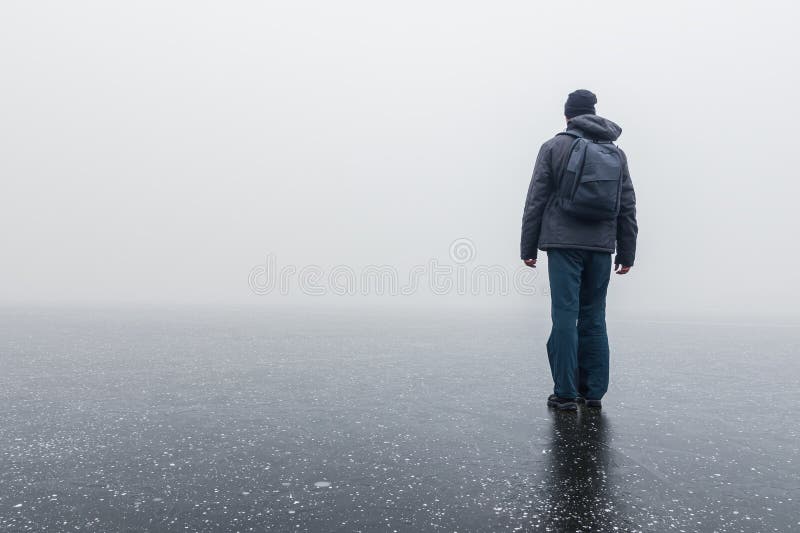A Man with a Backpack on His Back Standing on a Frozen Pond in the Fog ...