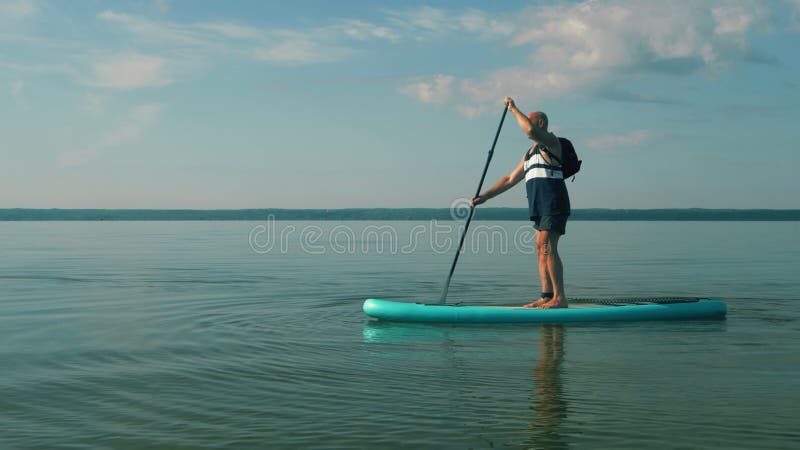 A Man with a Backpack on a SUP Board Swims in the Lake in the Evening ...