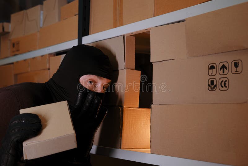 A Man in a Balaclava Takes a Box with a Parcel in a Warehouse at Night ...