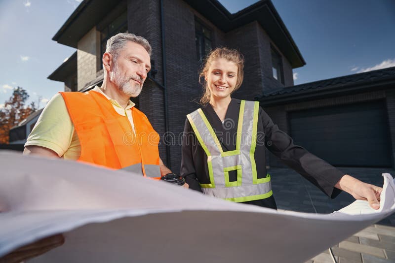 Aging Builder and Woman in Construction Vests Staring at Blueprints ...