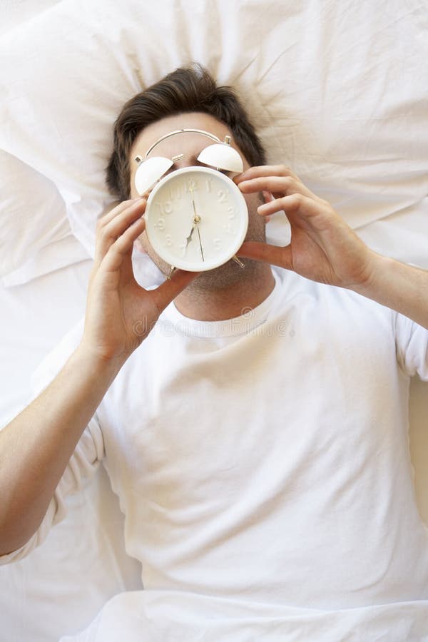 Man in Bed with Alarm Clock in Front of Face Stock Photo - Image of ...