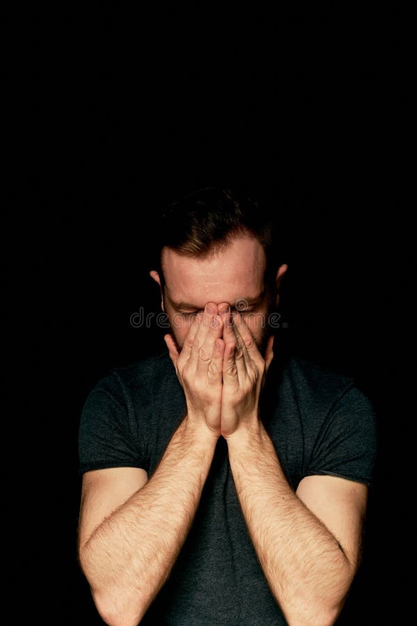 A Man on a Black Background Covers His Face with His Hands. the ...