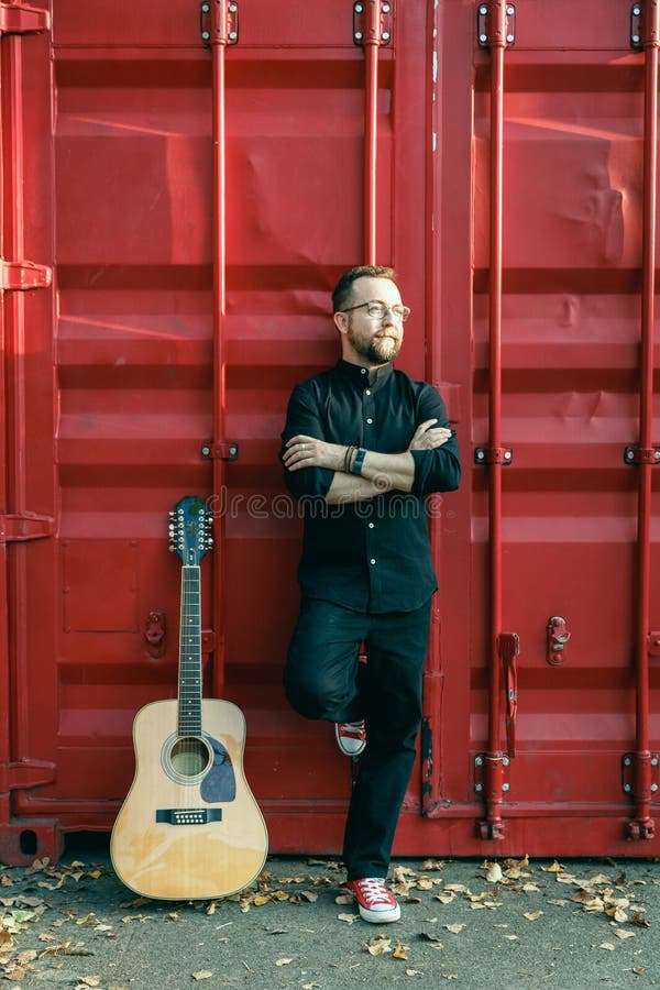 Man in Black Leaning Against the Red Container with Acoustic 12 String ...