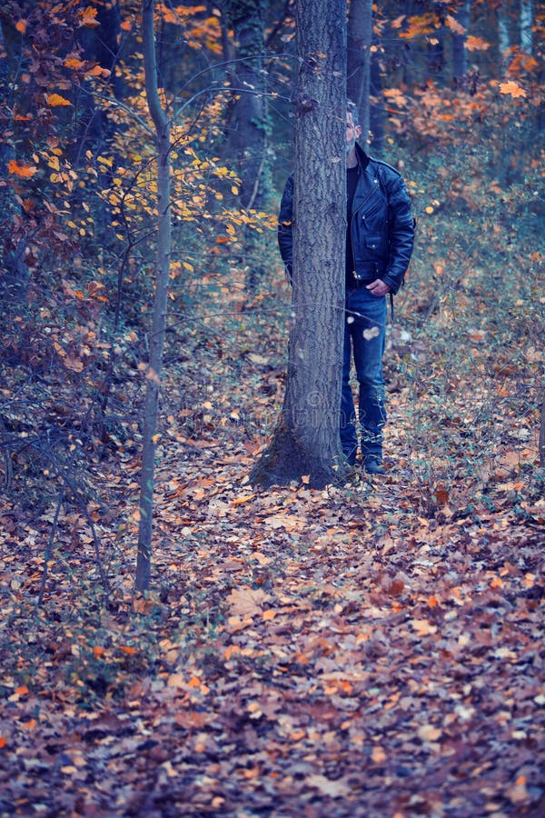 Man in Black Leather Jacket Standing Behind Tree in Forest Stock Image ...