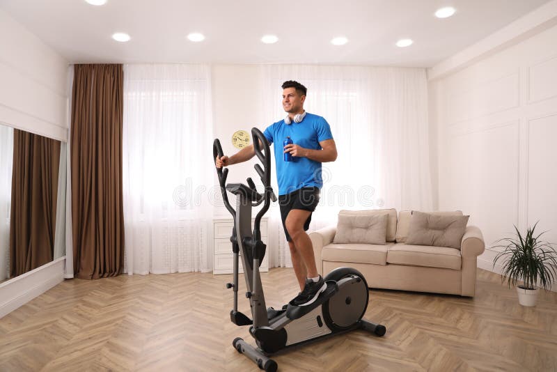Man with Bottle of Water Using Modern Elliptical Machine at Home Stock ...