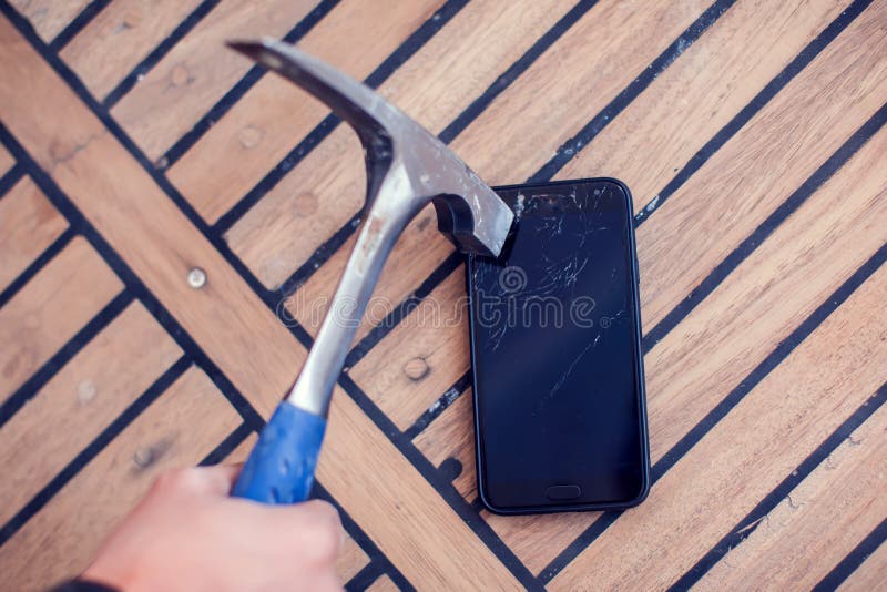 A Man is Breaking a Smartphone Lying on a Wooden Table with a Hammer ...