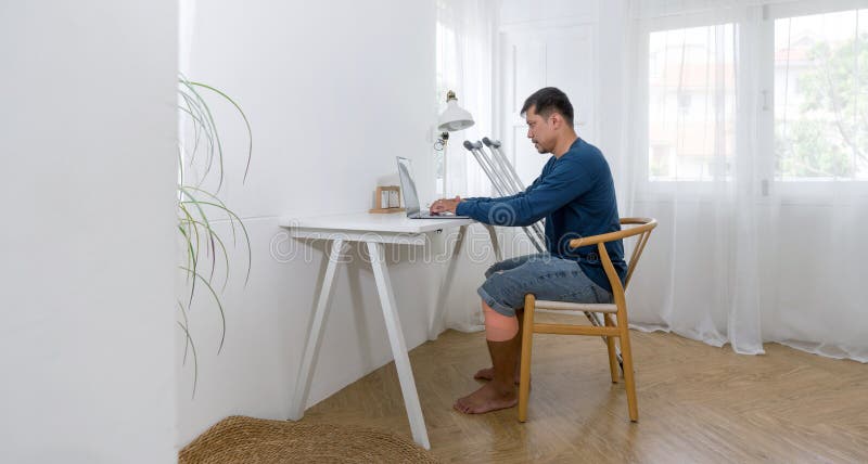 A Man with a Broken Leg Immersed in His Work, Sitting in an Office or Home-based Workstation ...