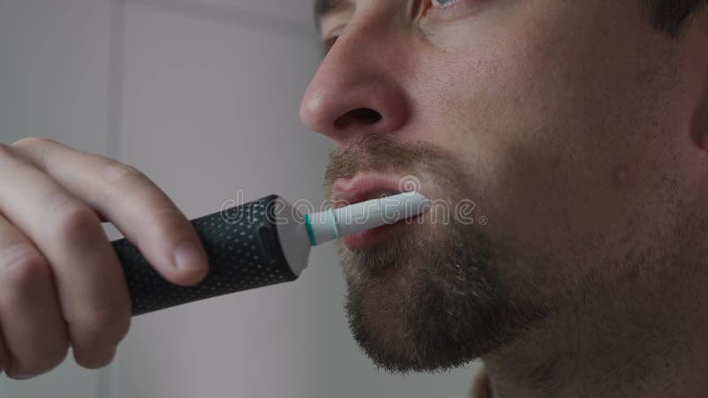 Man is Brushing His Teeth with an Electric Toothbrush in Bathroom As ...