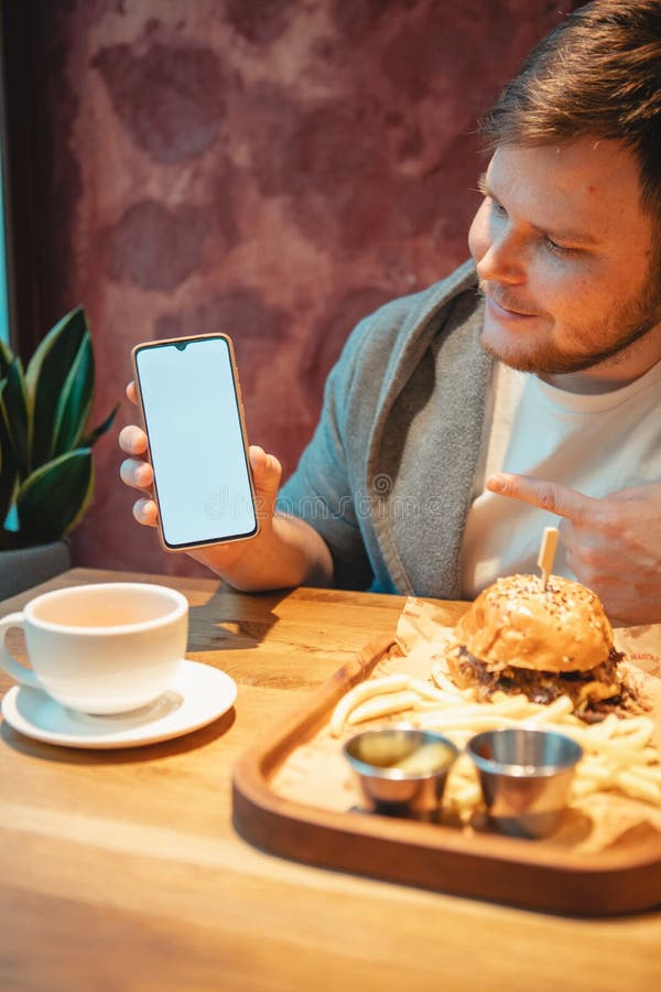 Man in Cafe Holding Phone with White Screen Eating Burger Stock Photo ...