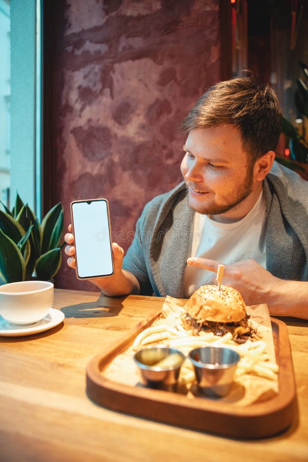 Man in Cafe Holding Phone with White Screen Eating Burger Stock Photo ...