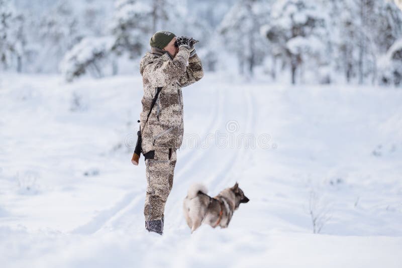 Man in Camouflage Gear with a Dog in a Snowy Forest, Using Binoculars ...