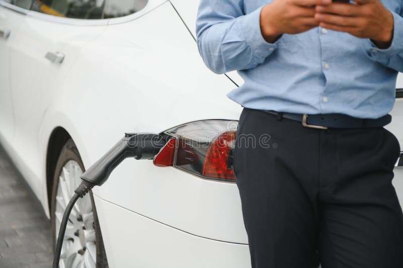 Man Charging His Electric Car at Charge Station and Using Smartphone ...