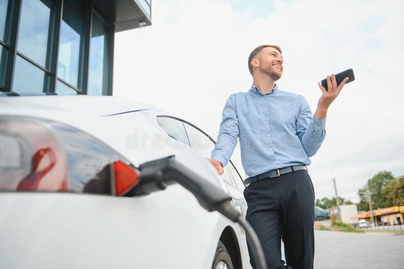 Man Charging His Electric Car at Charge Station and Using Smartphone ...