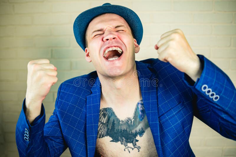 A Man with Chest Tattoo Wearing a Blue Jacket and a Hat Energetically ...