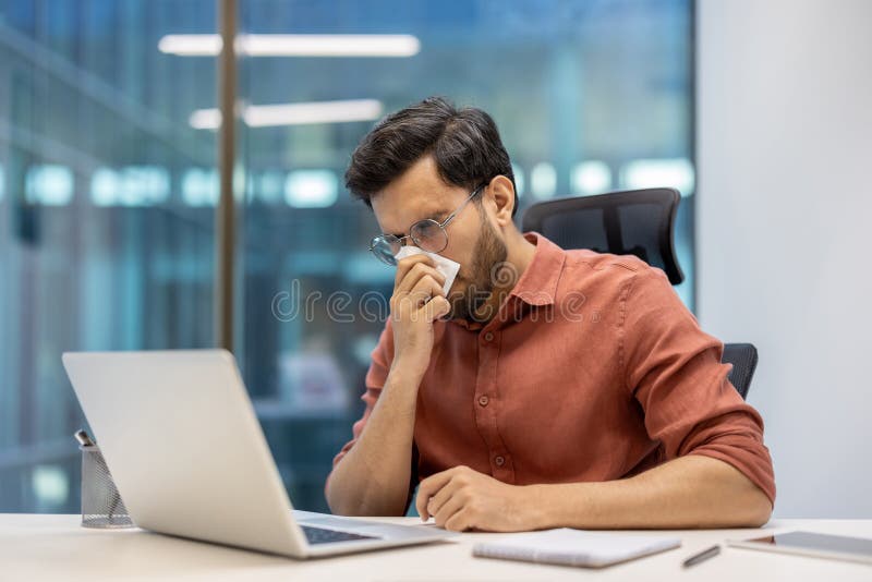 Man with Cold at Office Using Tissue while Working on Laptop in Modern ...