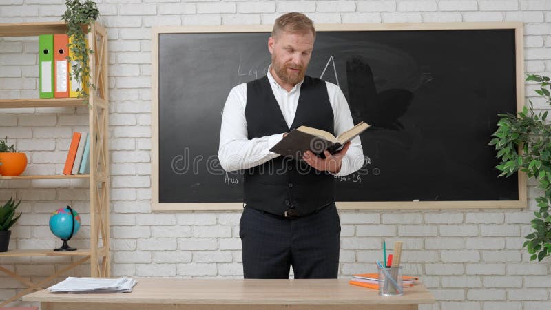 Man College Teacher at Desk in Classroom in Front of Chalkboard Holding ...