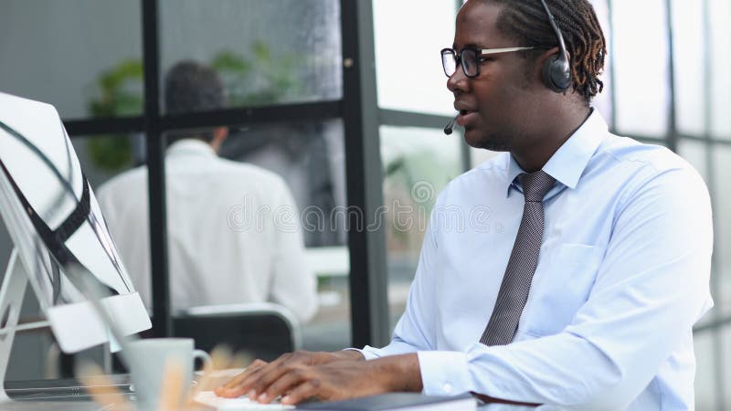A Man at a Computer in a Call Center Talking Using Headphones with a ...