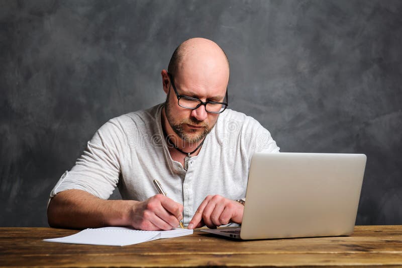 A Man at a Computer Writes in a Notebook. Stock Photo - Image of ...
