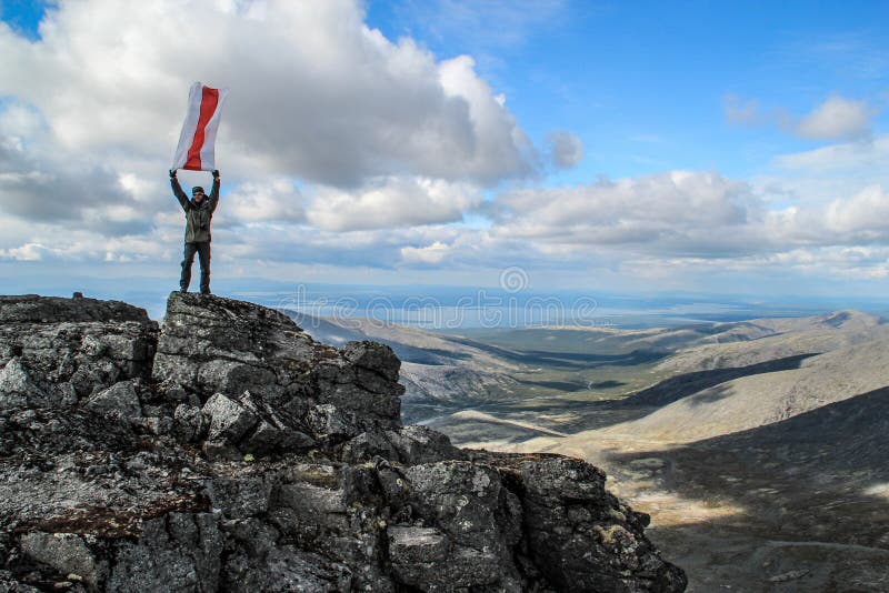 A Man Conquered the Top of the Mountains and Holds a Flag Flying Stock ...