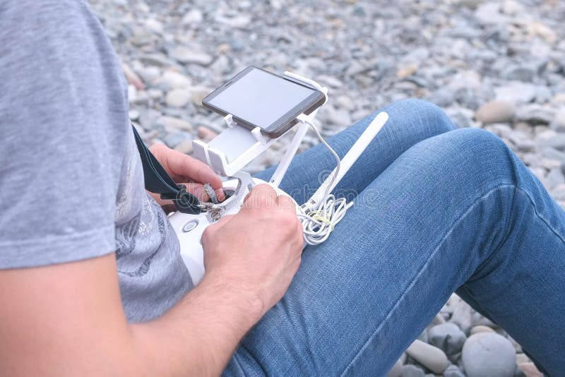 Man Controls a Drone with a Remote Control Sitting on a Stone Beach by ...