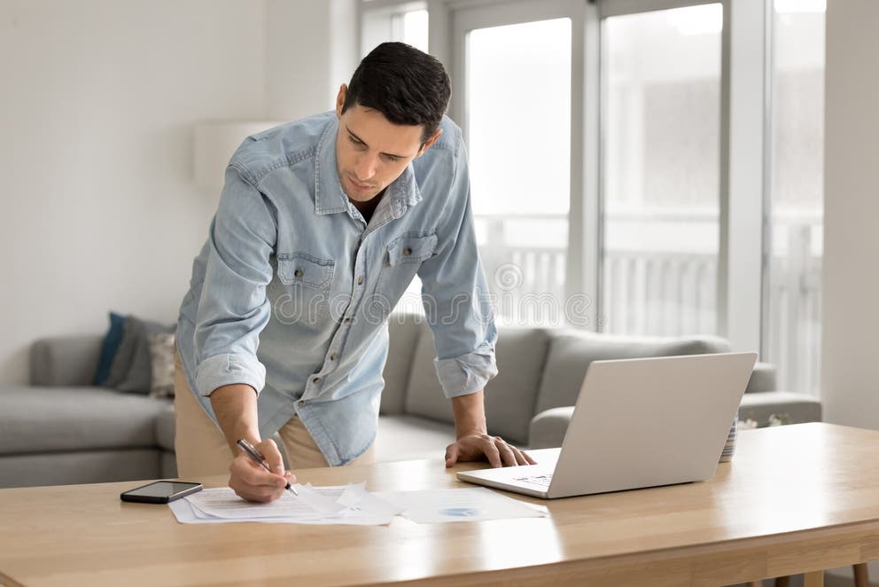 Man Leaning Over Desk, Making Notes, Focused on Paperwork Stock Photo ...