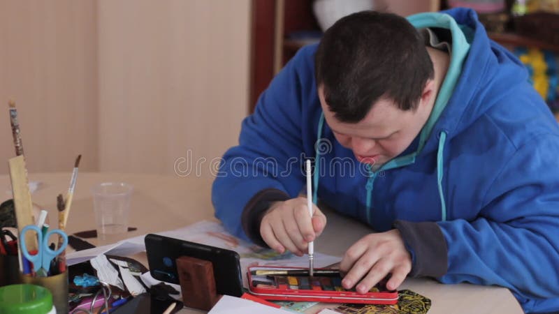 A Man with Down Syndrome is Engaged in Drawing Sitting on a Table in ...