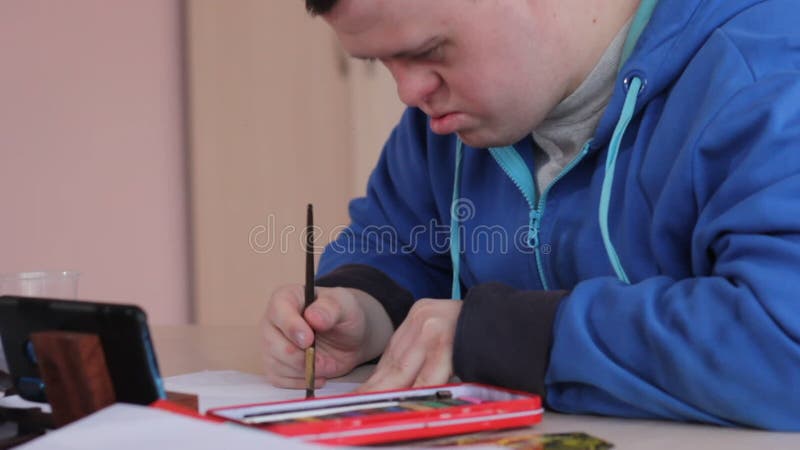 A Man with Down Syndrome is Engaged in Drawing Sitting on a Table in ...