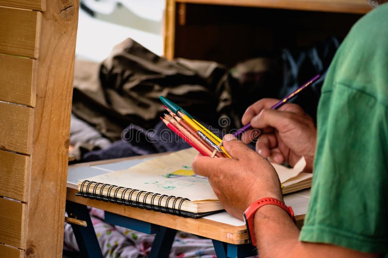 Man Drawing on a Notebook and Holding Pencils on a Table in a Converted ...
