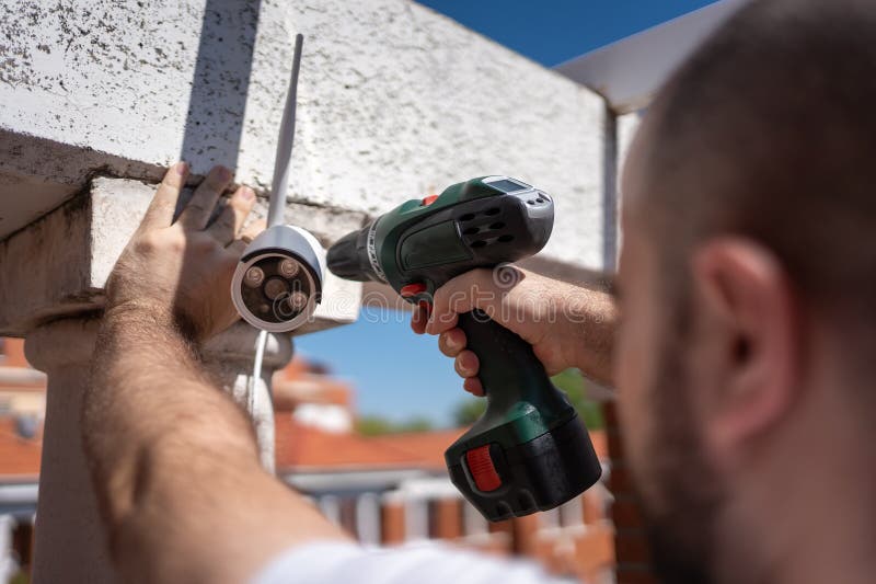 Man with a Drill Installing Security Cameras for Surveillance in a ...