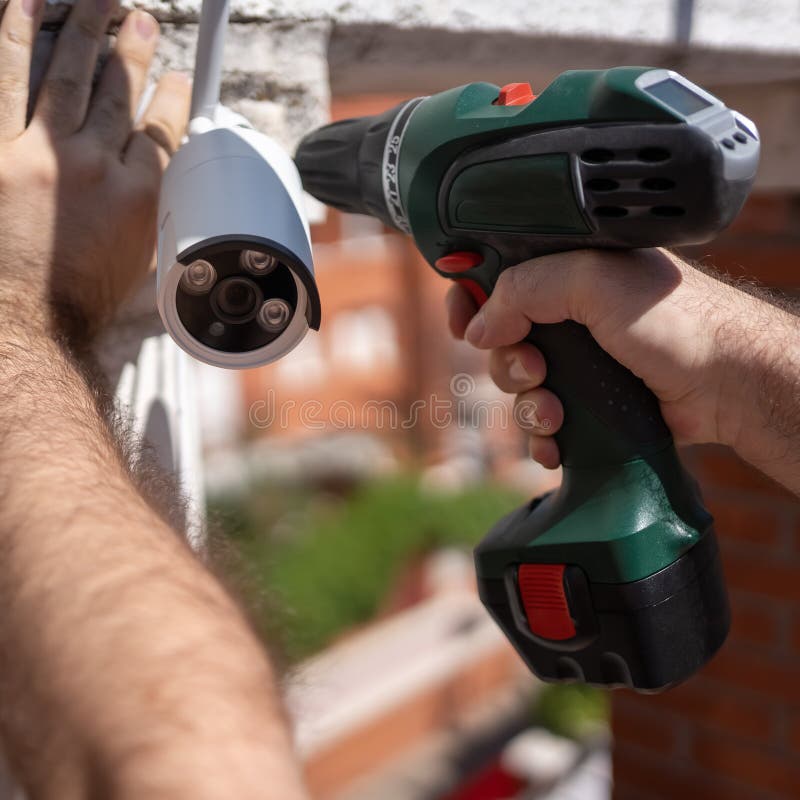 Man with a Drill Installing Security Cameras for Surveillance in a ...