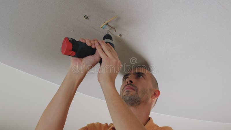 A Man Using a Handheld Portable Drill Drills Holes in the Ceiling for ...