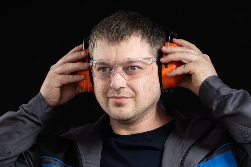 A Man in Earmuffs, Glasses and Overalls on a Black Background. Stock ...