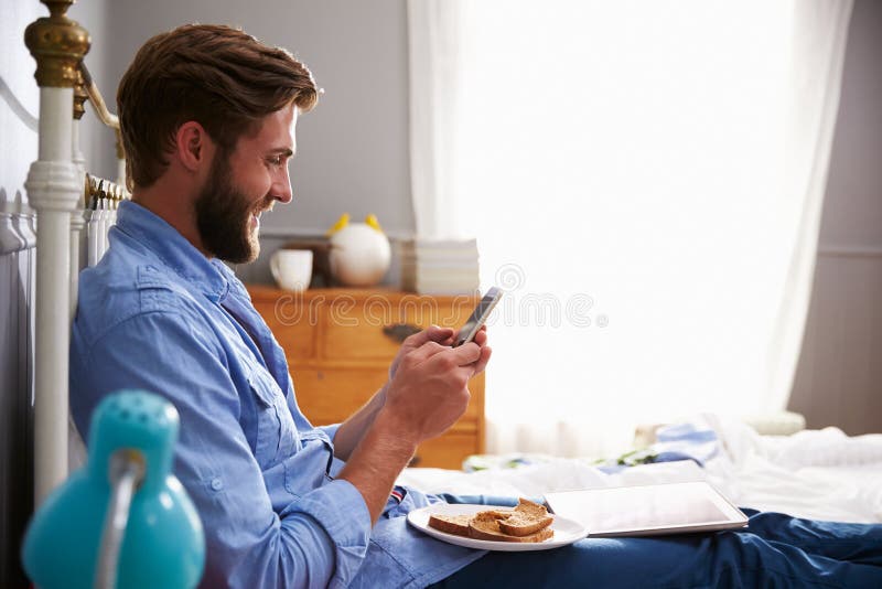 Man Eating Breakfast in Bed Whilst Using Mobile Phone Stock Photo ...