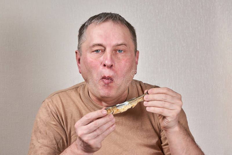 Man Eating Fried Smelt Fish Holding Fish with Hands in Front of Face ...