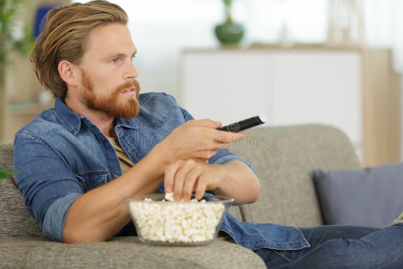 Man Eating Popcorn while Changing Channel with Remote-control Stock ...