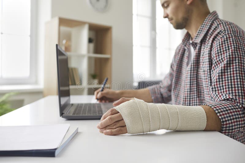 Man with Elastic Bandage on His Hand Sitting at Table, Working on ...