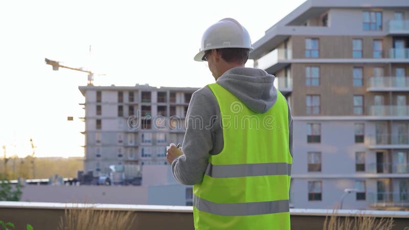 Man Engineer with a White Protective Helmet and Safety Vest is Writing ...