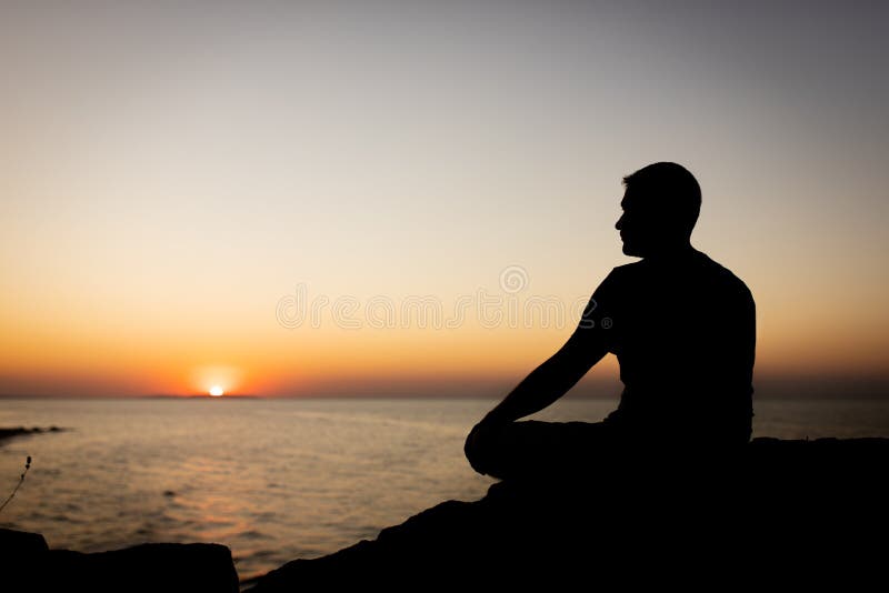 A Man Enjoys the View of the Sunset on the Sea, Sitting on a Rock ...