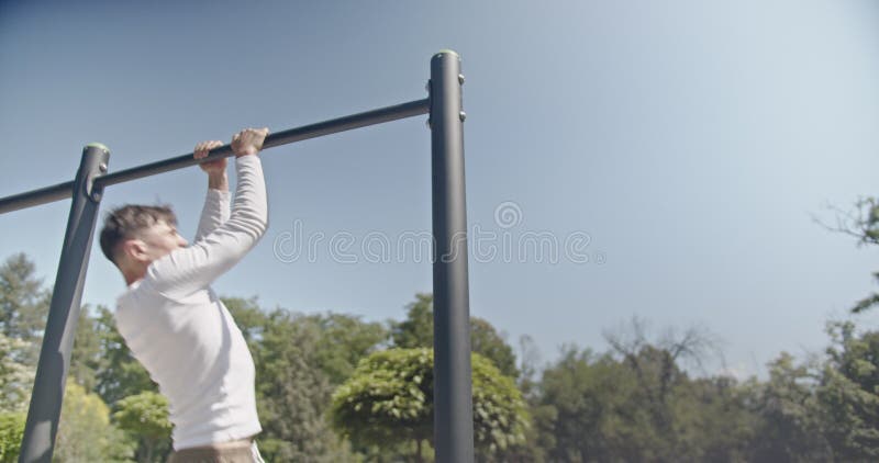 Man Exercising on Parallel Bars in the Park, Performing Pull-ups Under ...