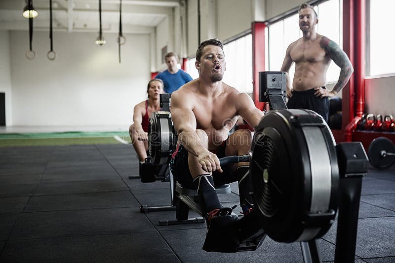 Man Exercising on Rowing Machine while Instructor Looking at Him Stock ...