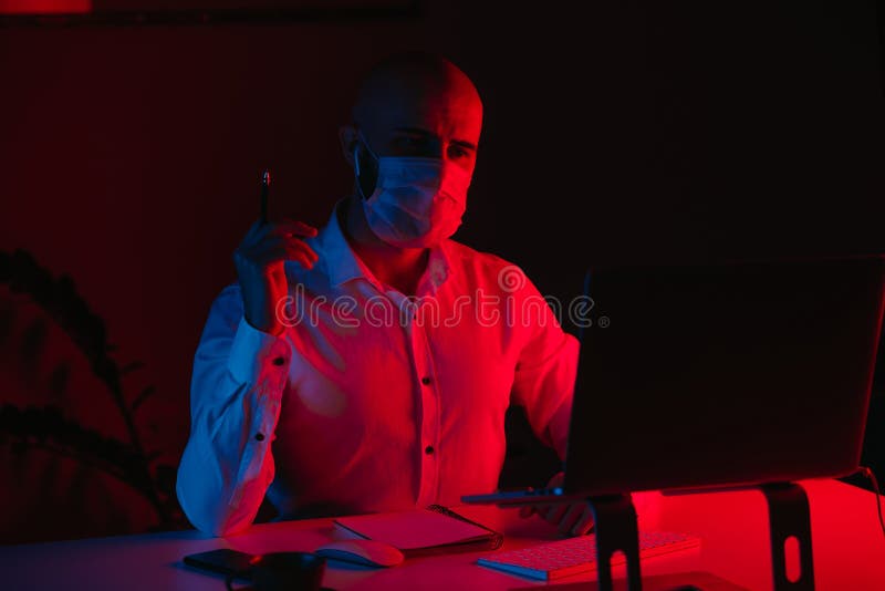 Man in a Face Mask with a Pen in Front of the Computer Under Blue and ...