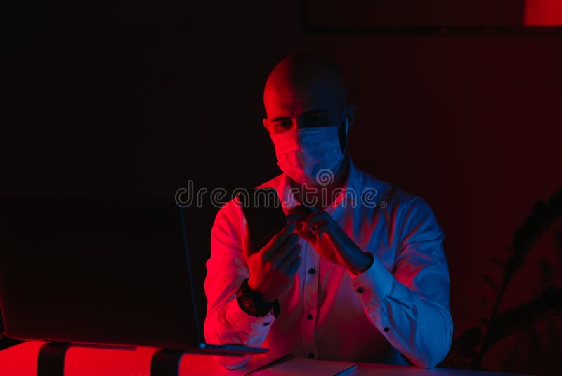 Man in a Face Mask with a Pen in Front of the Computer Under Blue and ...